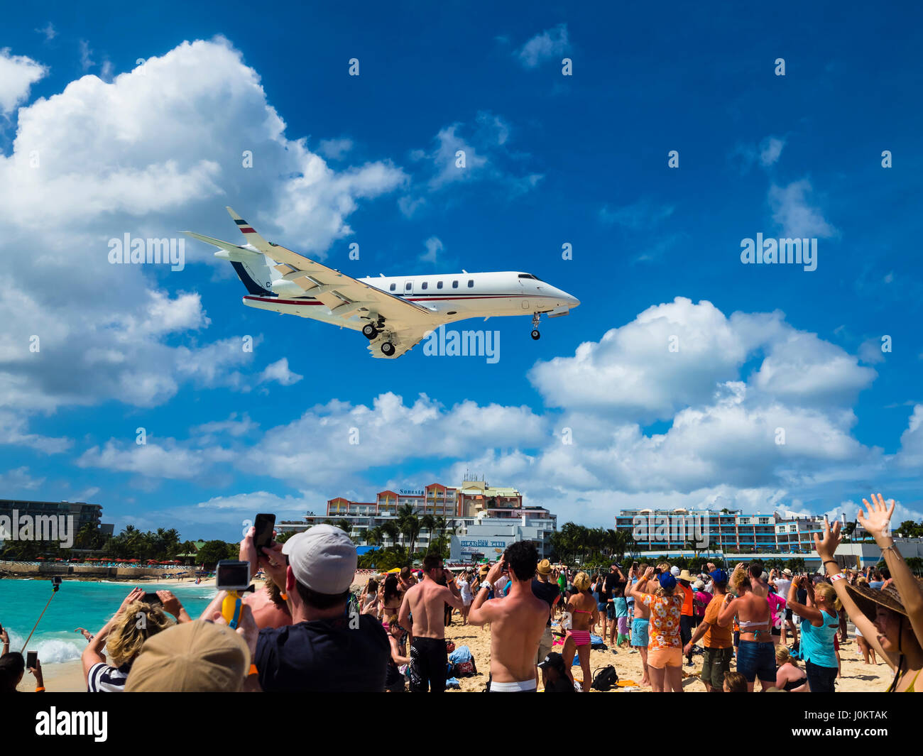 Tourists watching and photographing an airplane landing over Maho Beach ...