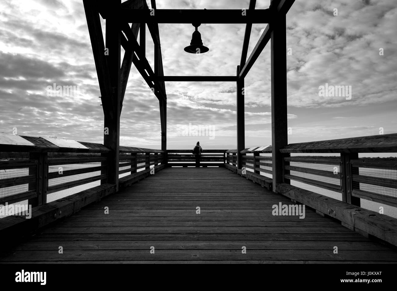 Lone person standing at end of pier looking into clouds and body of ...