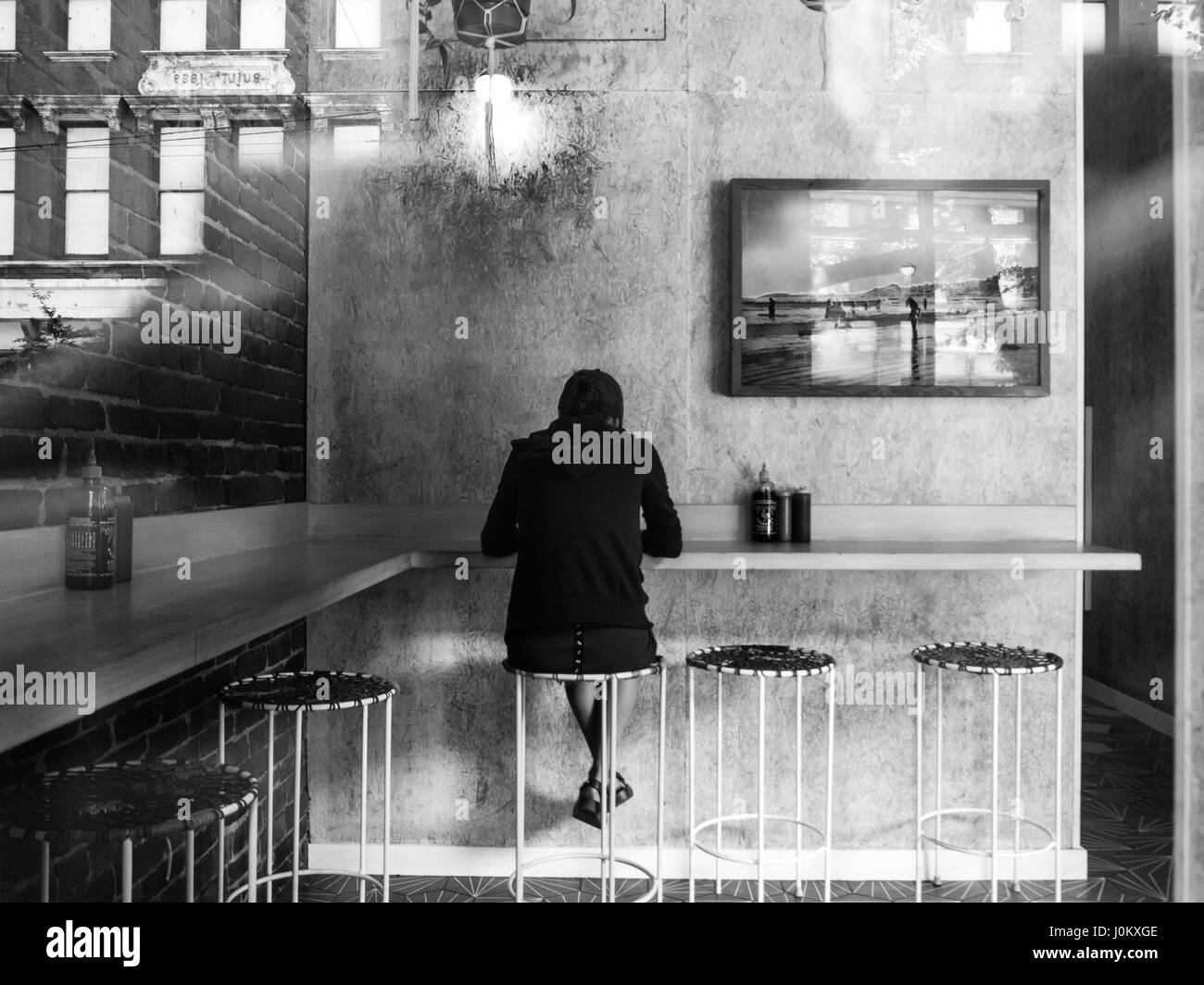 Woman sitting at a bar in a cafe with reflections from the outside ...