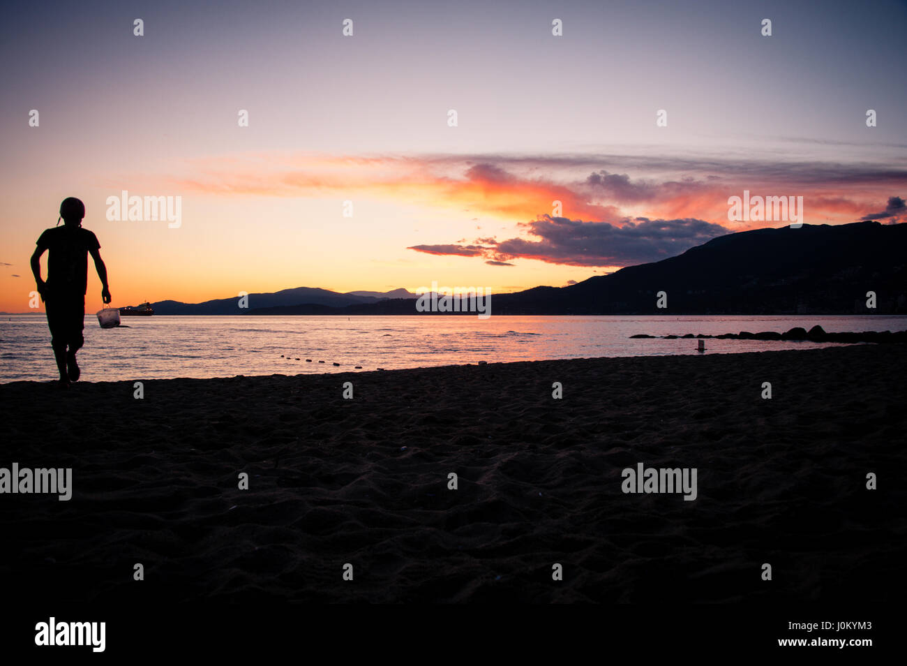 Silhouetted man carrying a pale, against sunset on beach Stock Photo ...