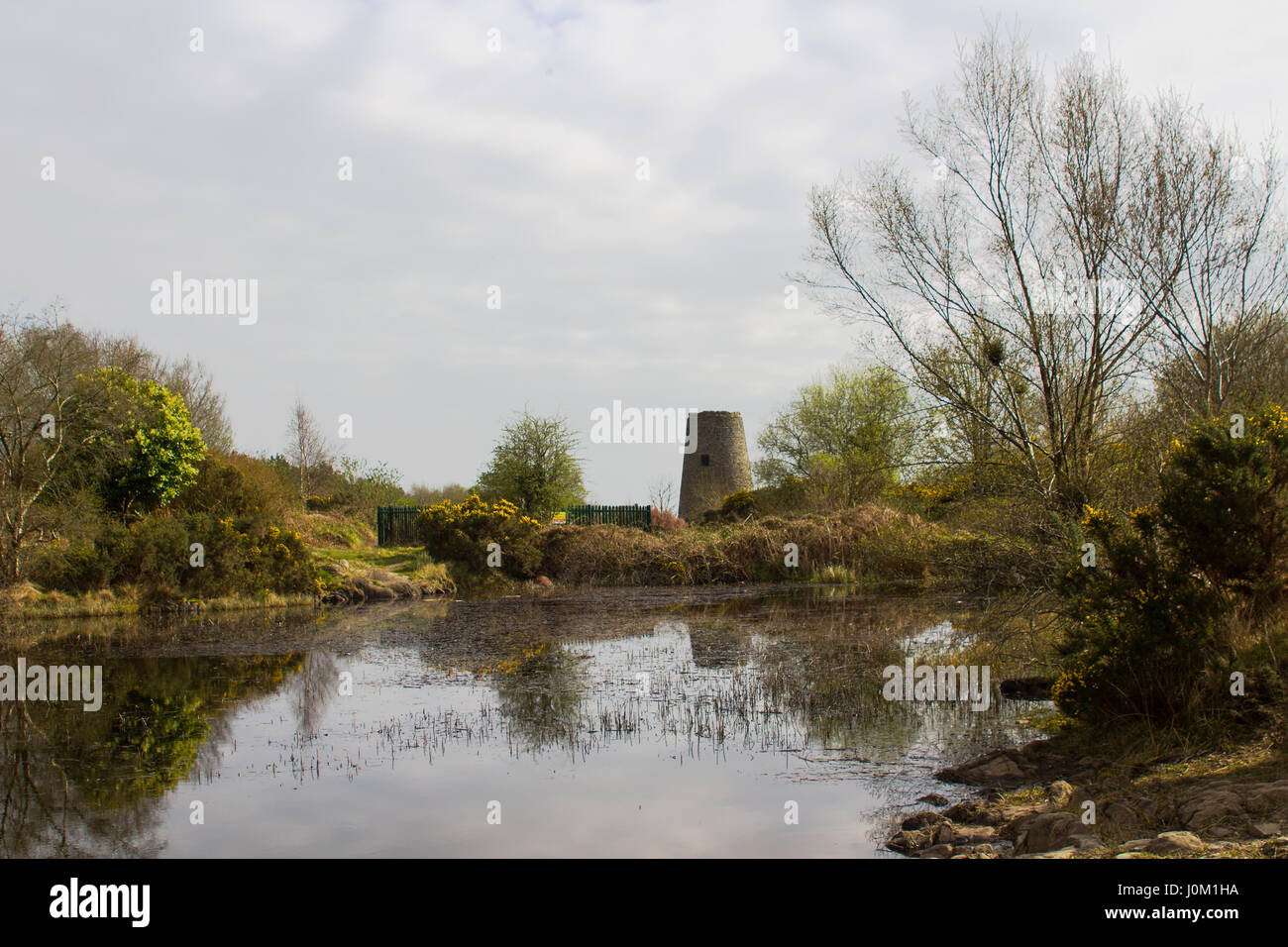 An old windmill stump reflected in the still water of the lake in the ...