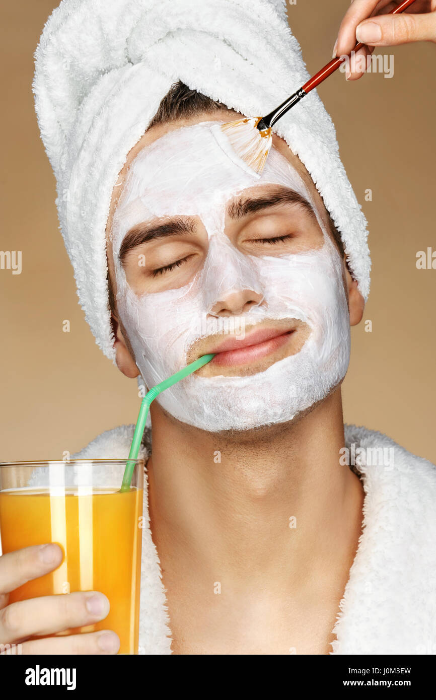 Handsome man getting a facial treatment. Beautician is applying facial ...