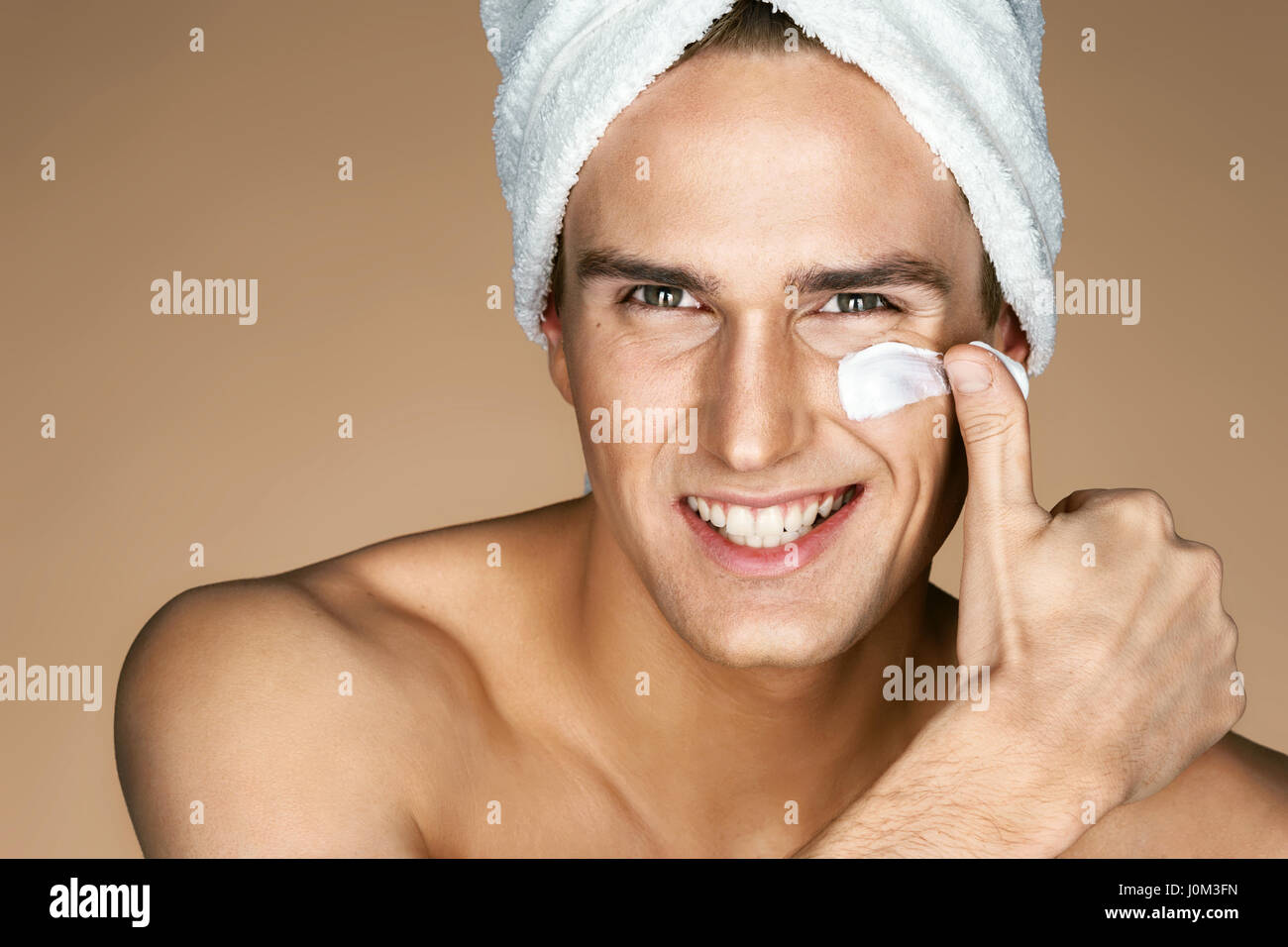 Young man applying cream to his face. Portrait of smiling man with ...