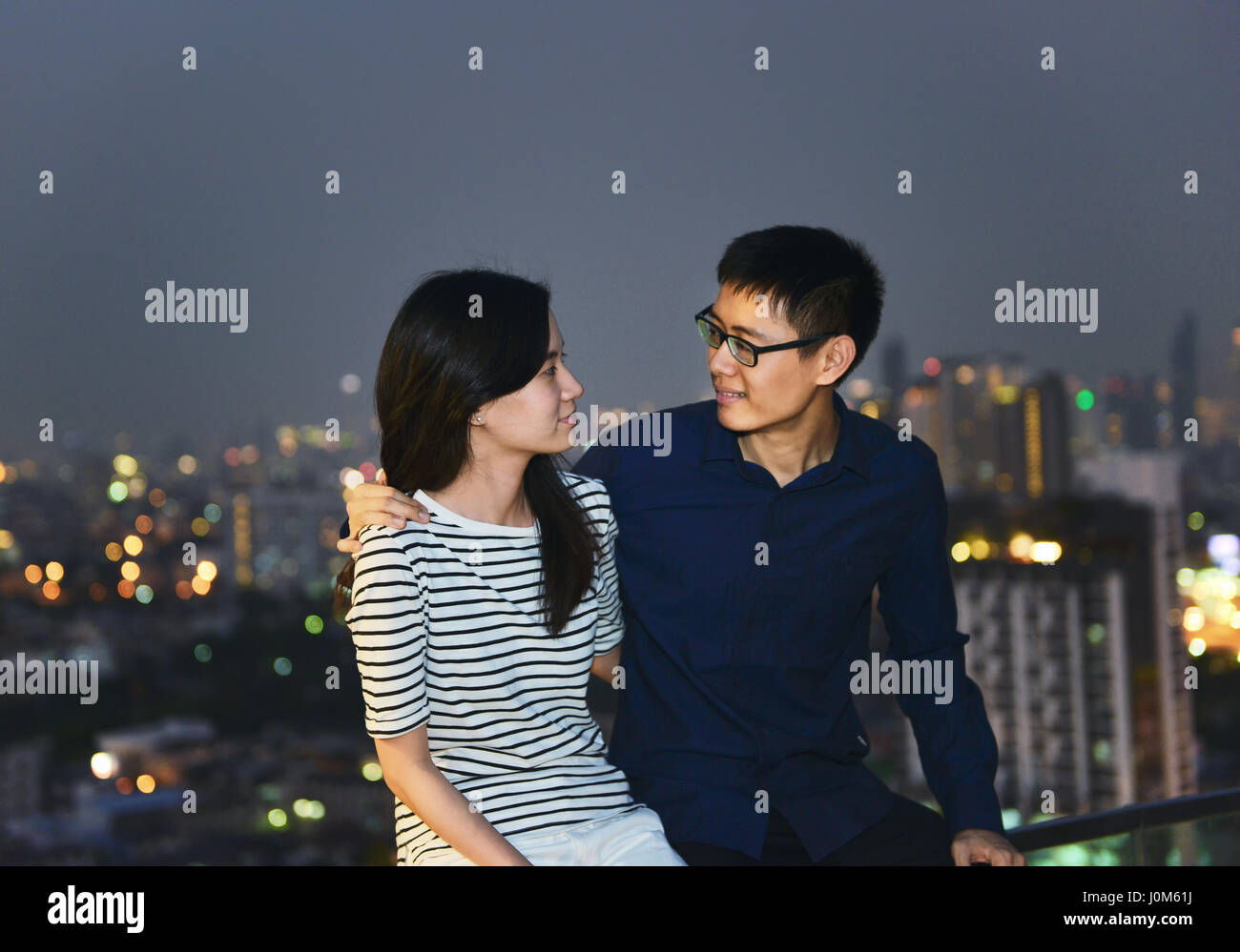 Asian Couple looking each other on rooftop with city background ...