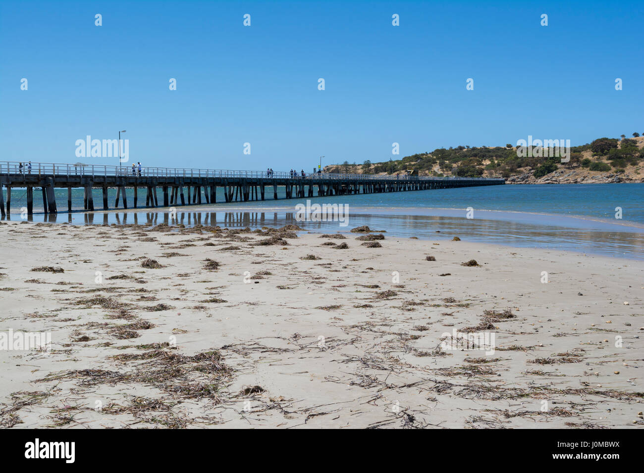 People walking along the Victor Harbor jetty, which is reflected in the ...