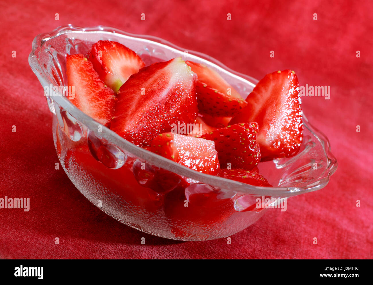 Fresh strawberries in glass bowl on red textile background. Oblique ...