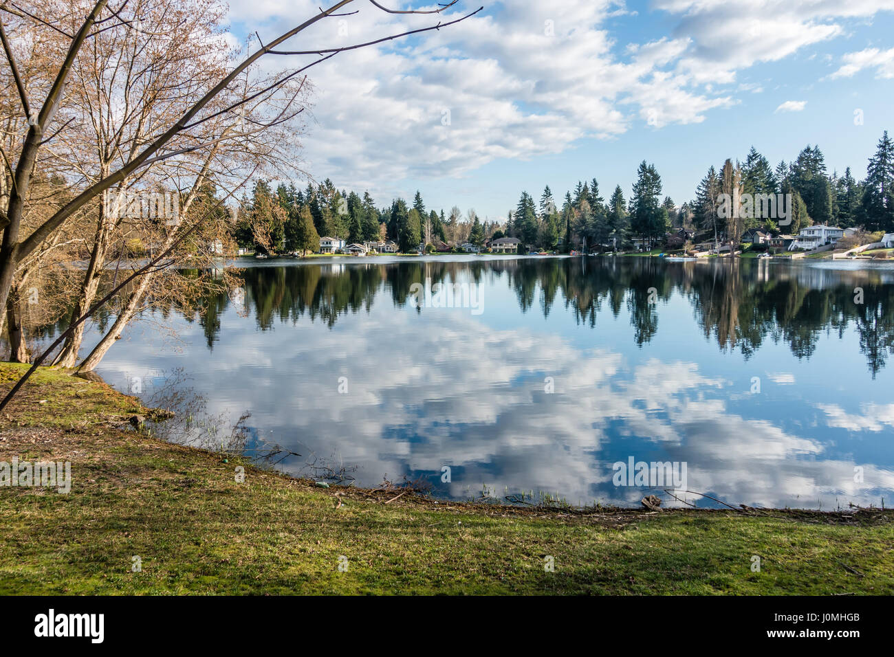 Homes, trees and sky are reflected in the water of Mirror Lake in ...