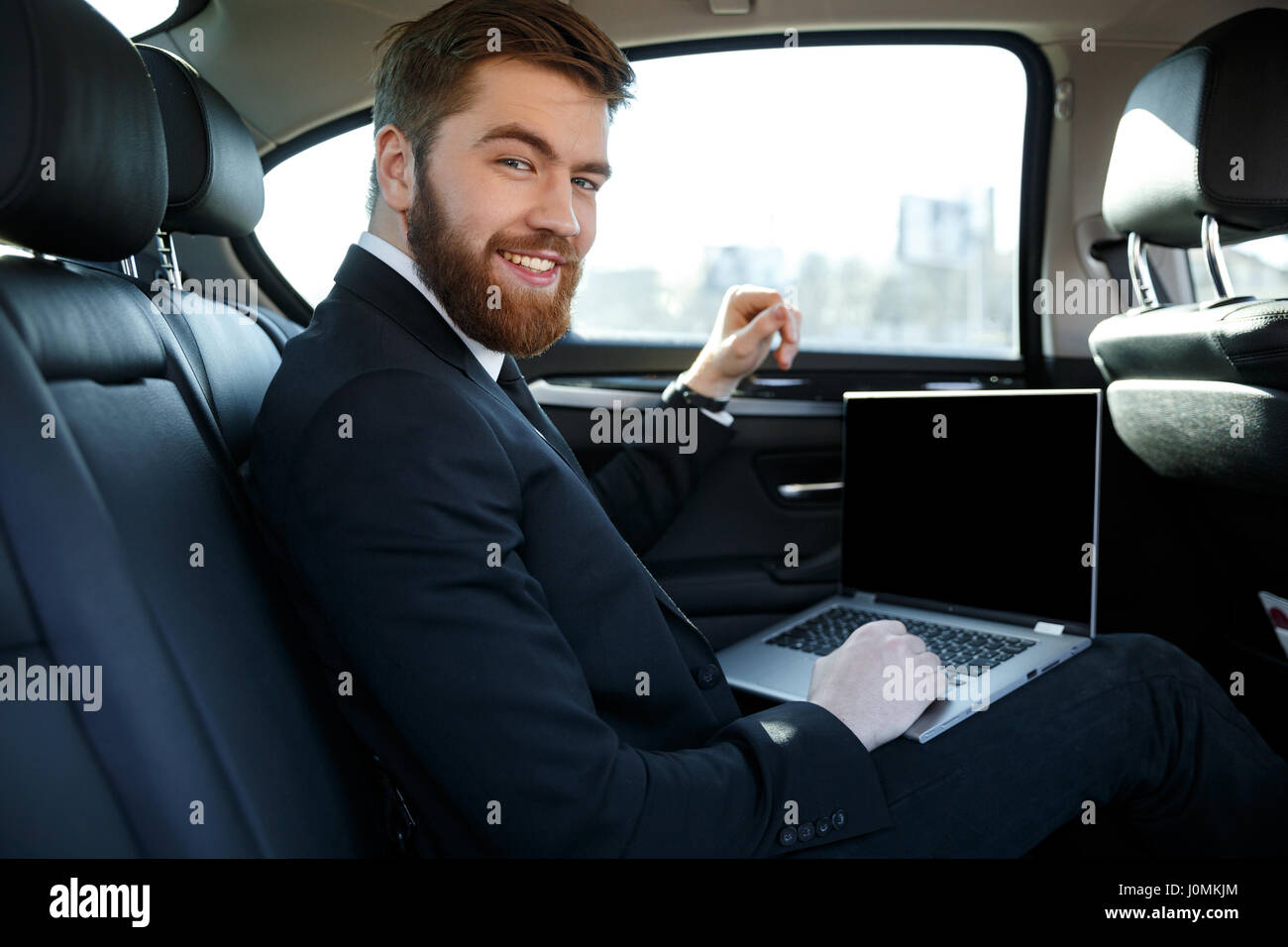 Side view of smiling business man sitting on back seat of a car with ...