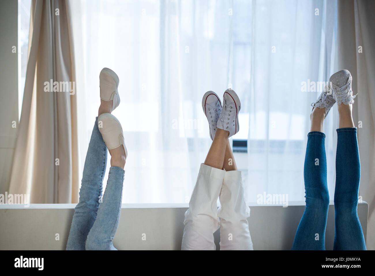 Partial view of three young women lying on sofa with legs up Stock ...