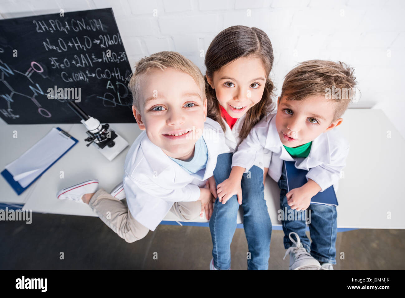 Overhead view ot three kids in white coats smiling at camera Stock ...