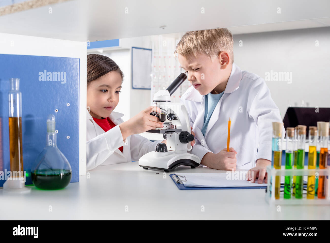 Little boy and girl in white coats using microscope in chemical ...