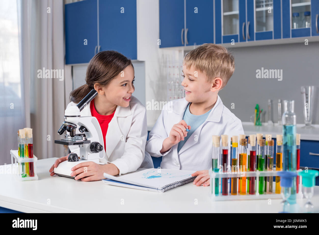 Little boy and girl in white coats using microscope and looking at each ...