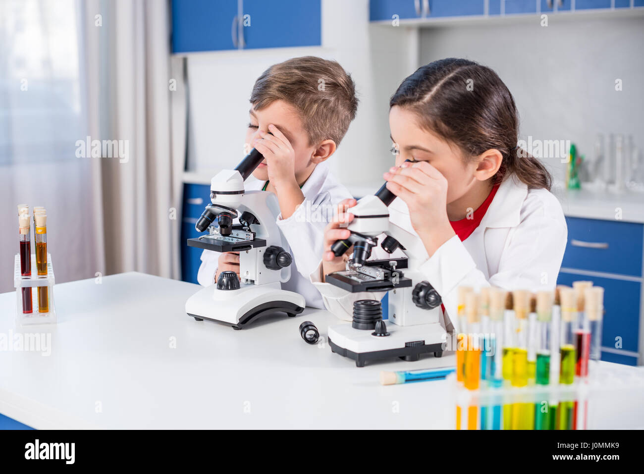 Little boy and girl in white coats using microscopes in chemical ...