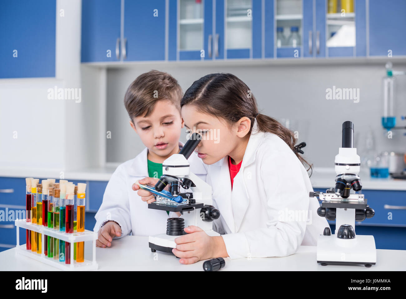Little boy ang girl in white coats using microscope in chemical ...