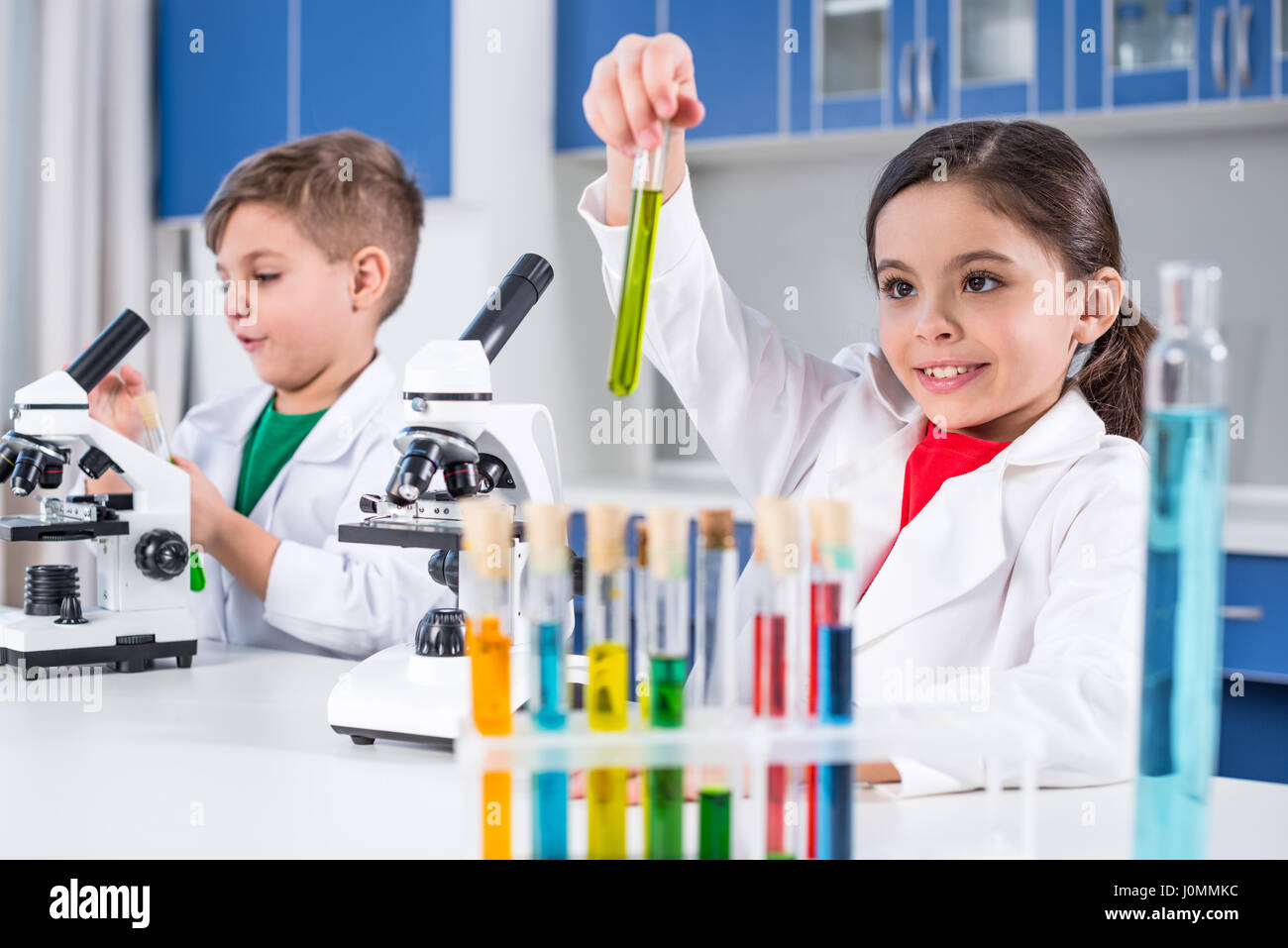 Little boy and girl in white coats using microscopes and reagents in chemical laboratory Stock ...