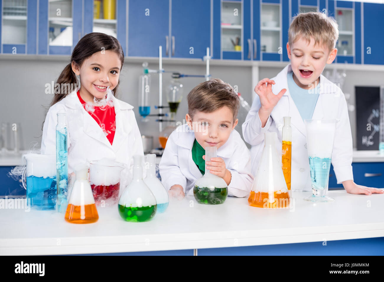 Three kids in white coats making chemical experiment in laboratory ...