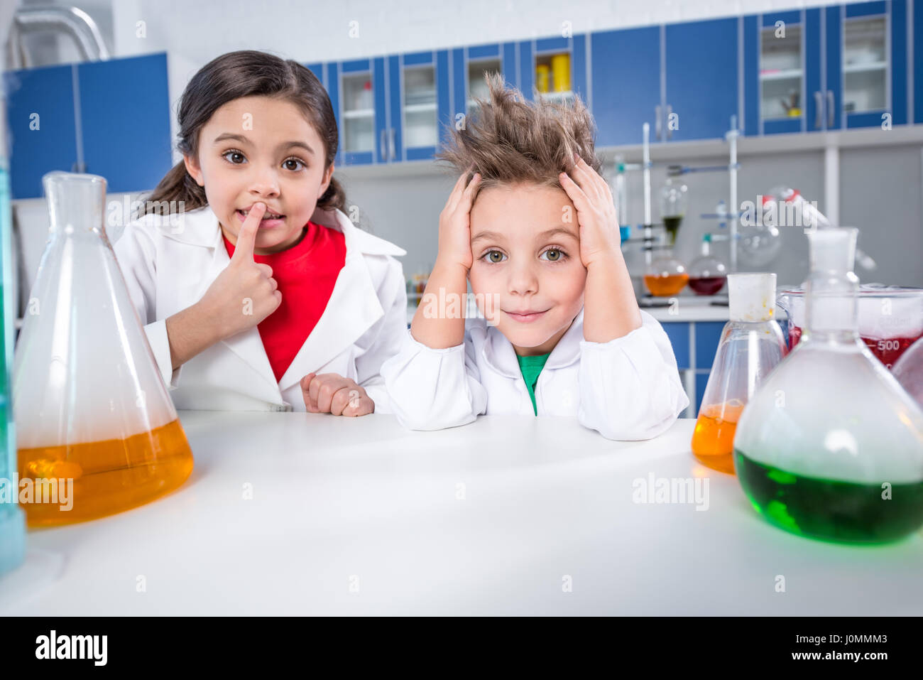 Boy and girl in lab coats looking at camera in chemical laboratory ...