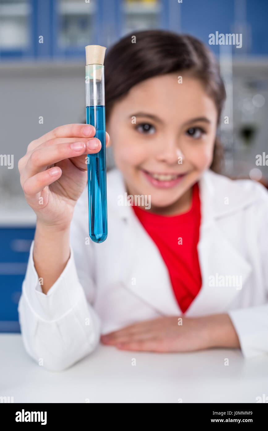 Happy little girl showing test tube with reagent and smiling at camera ...