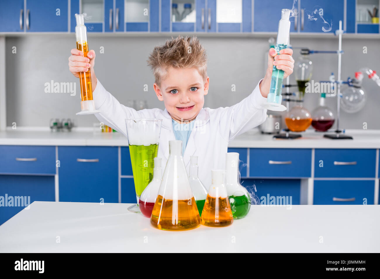 Cute little boy in lab coat holding flasks with reagents and smiling at ...