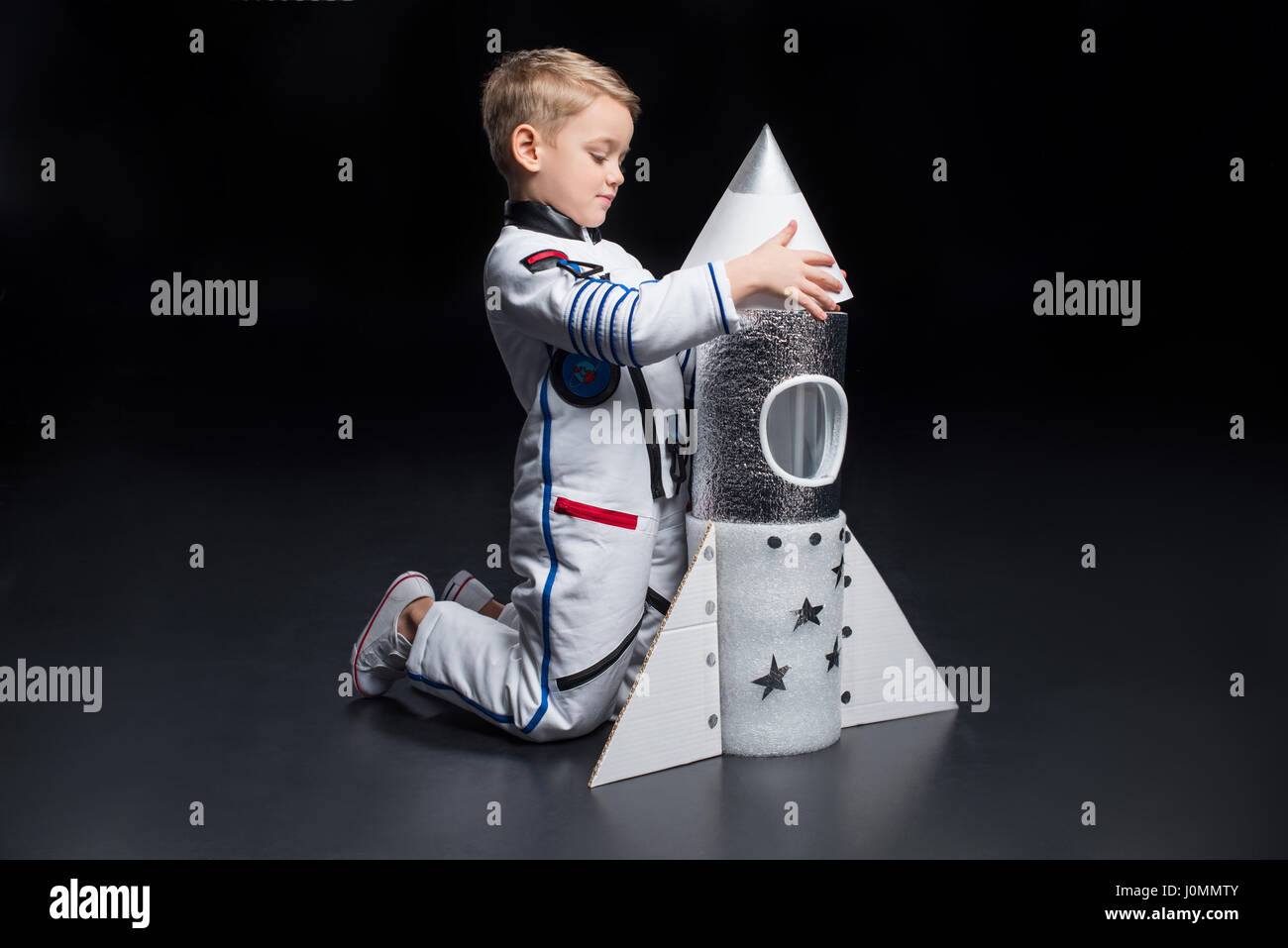 Little boy astronaut in space suit kneeling near rocket and playing ...