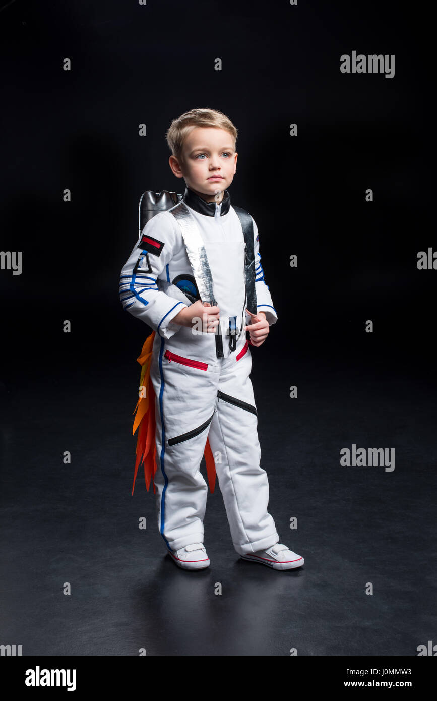 Little boy astronaut in space suit standing and looking away on black ...