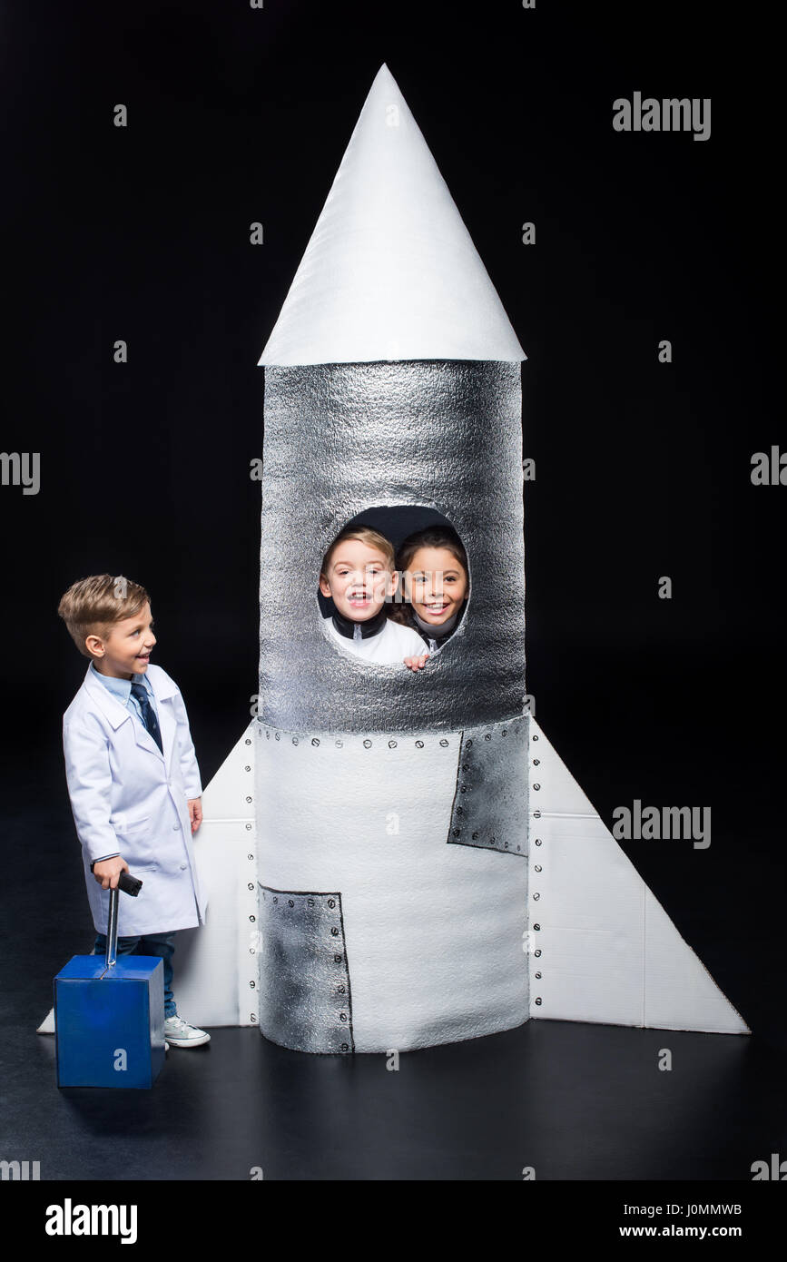 Three smiling little kids playing astronauts with spaceship on black ...