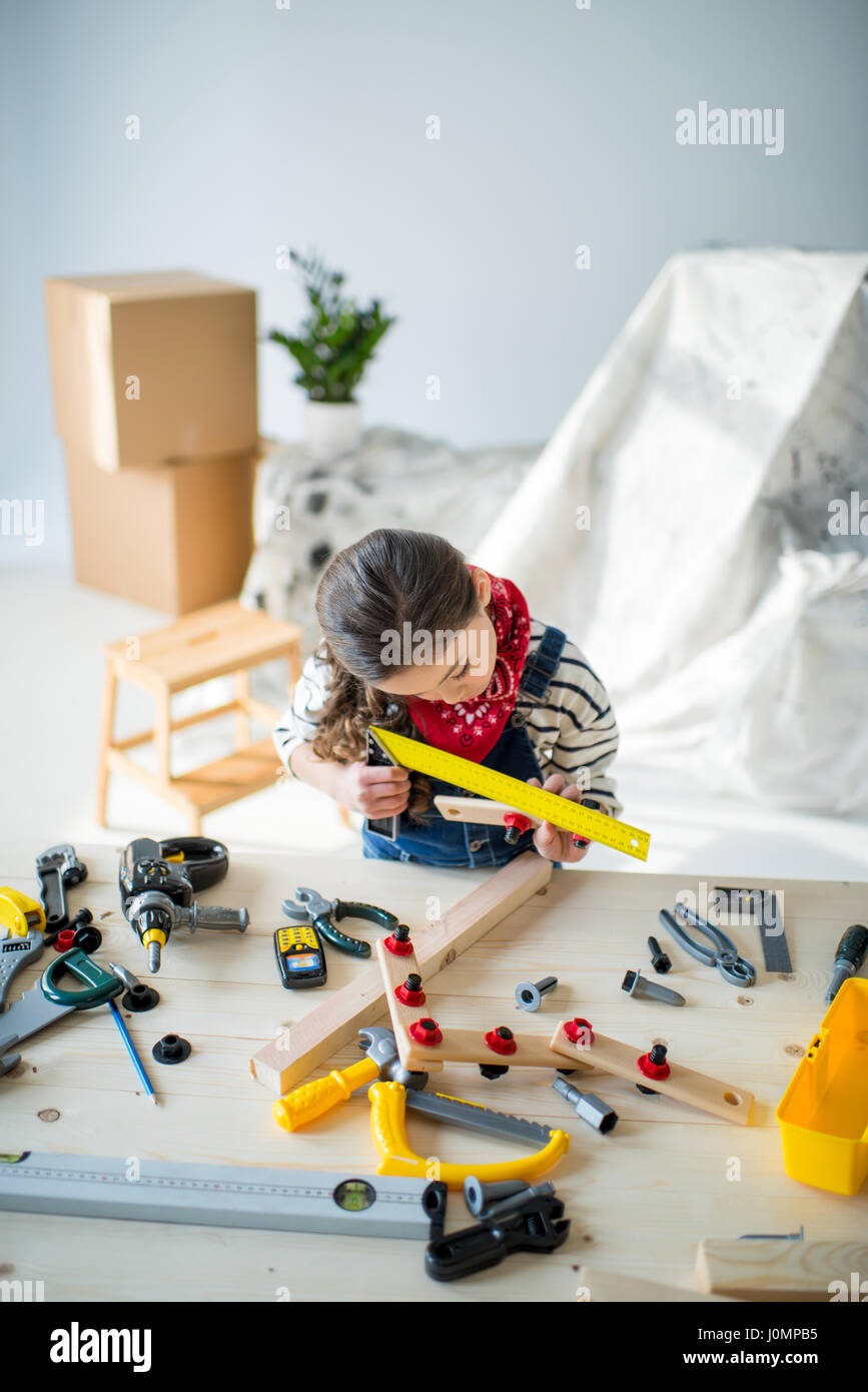Cute little girl leaning on table with toy tools and measuring plank ...