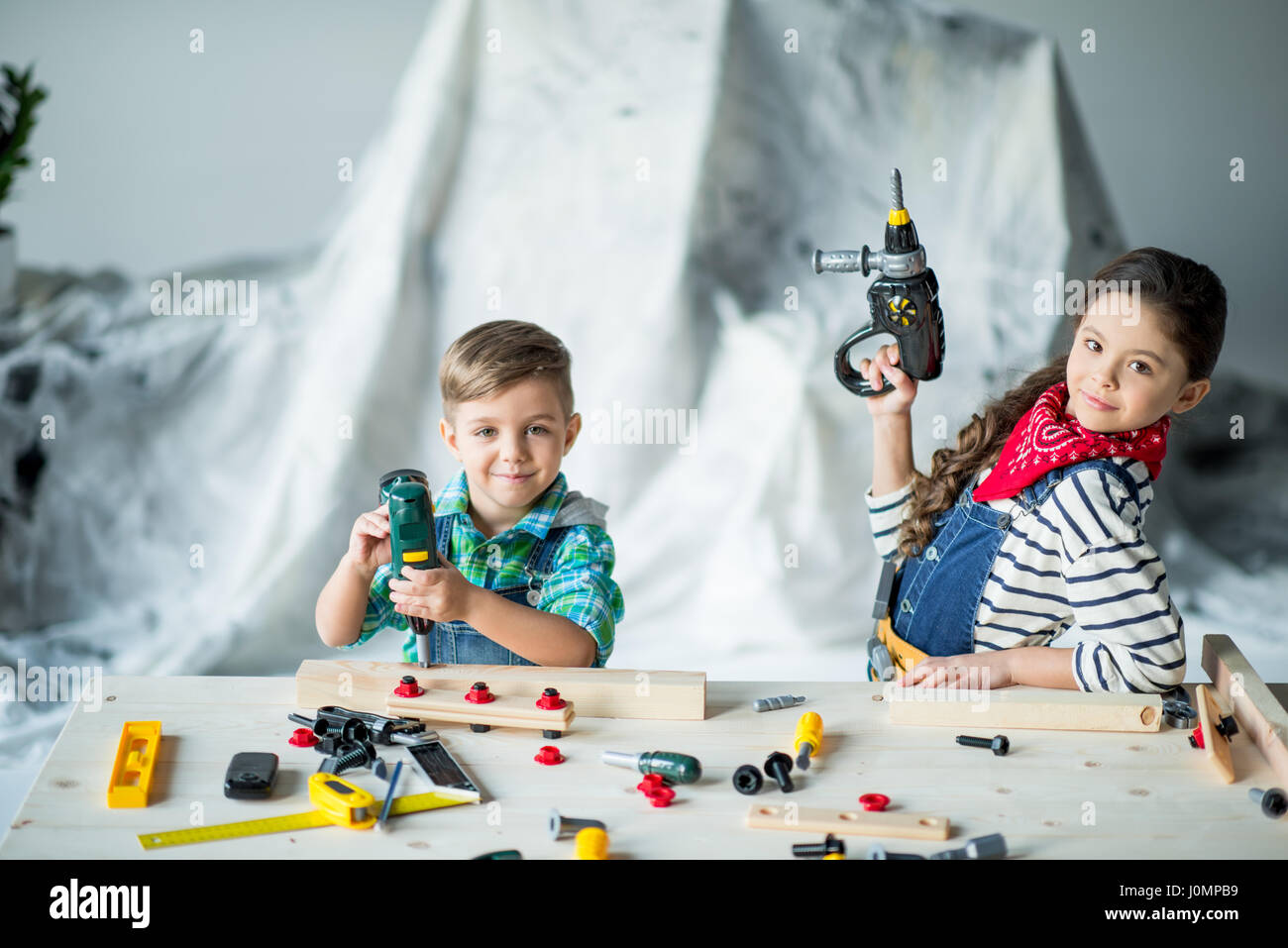 Cute boy and girl playing with toy tools in workshop and smiling at ...
