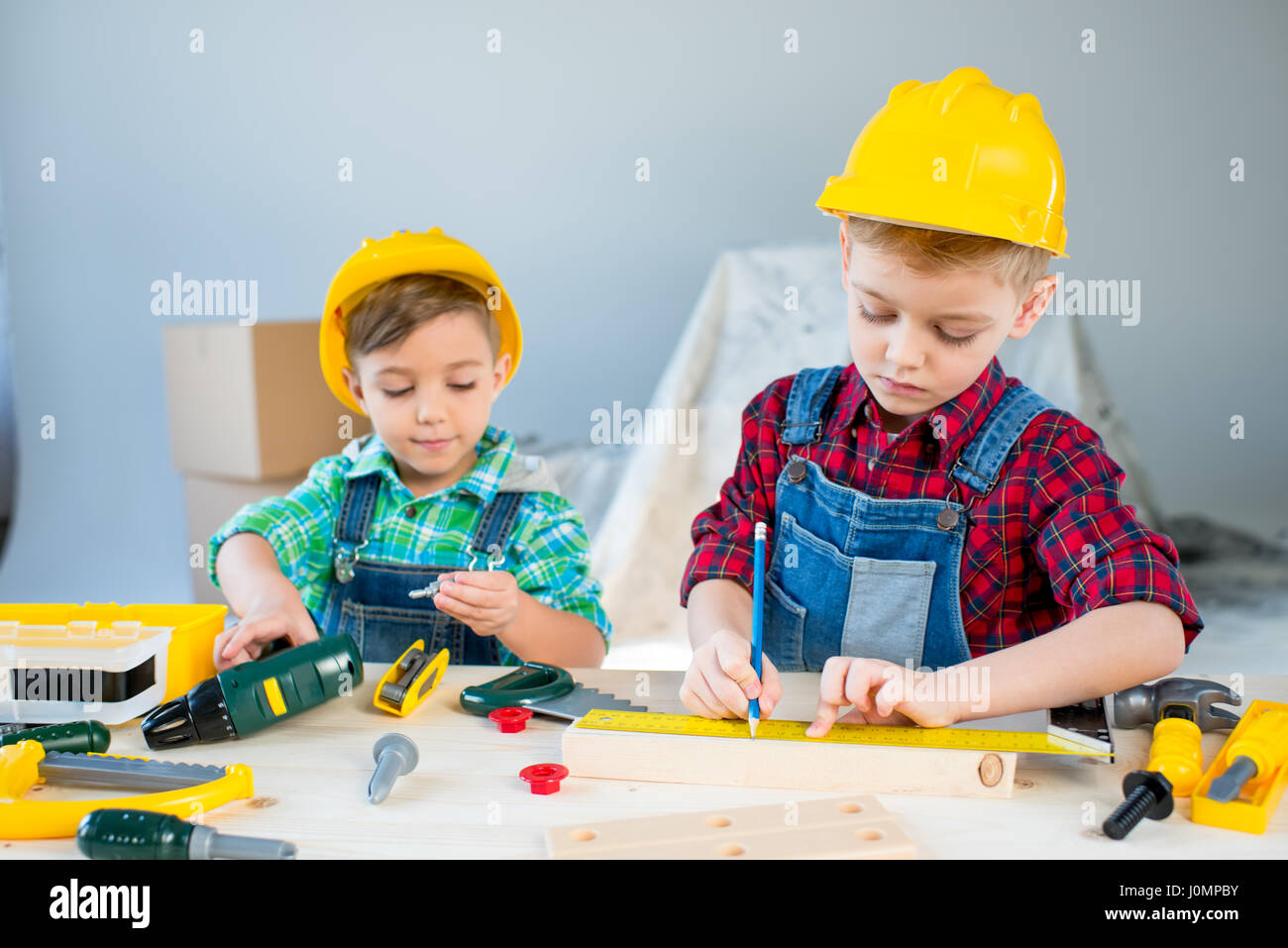 Two little boys in yellow hard hats playing with toy tools in workshop ...