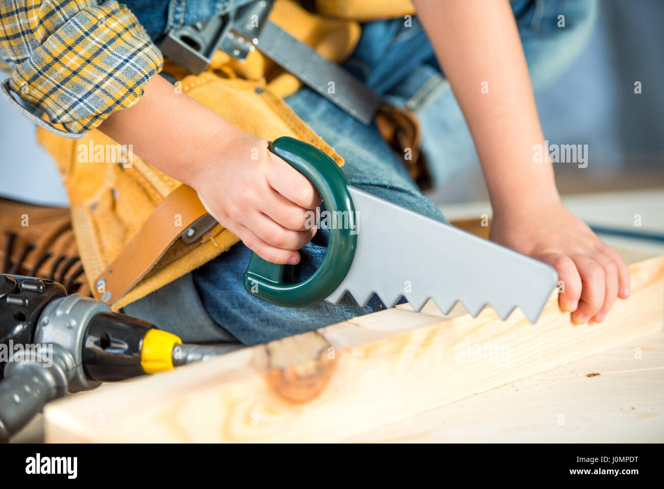 Close-up partial view of little boy sawing wooden plank with toy saw ...