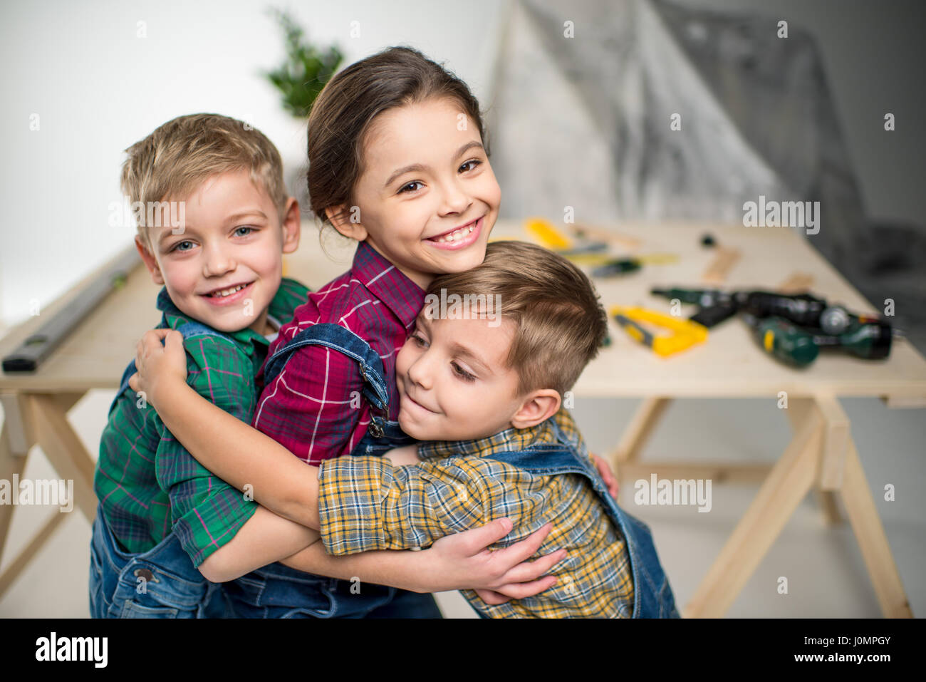 Two little boys and girl hugging in workshop and smiling at camera ...