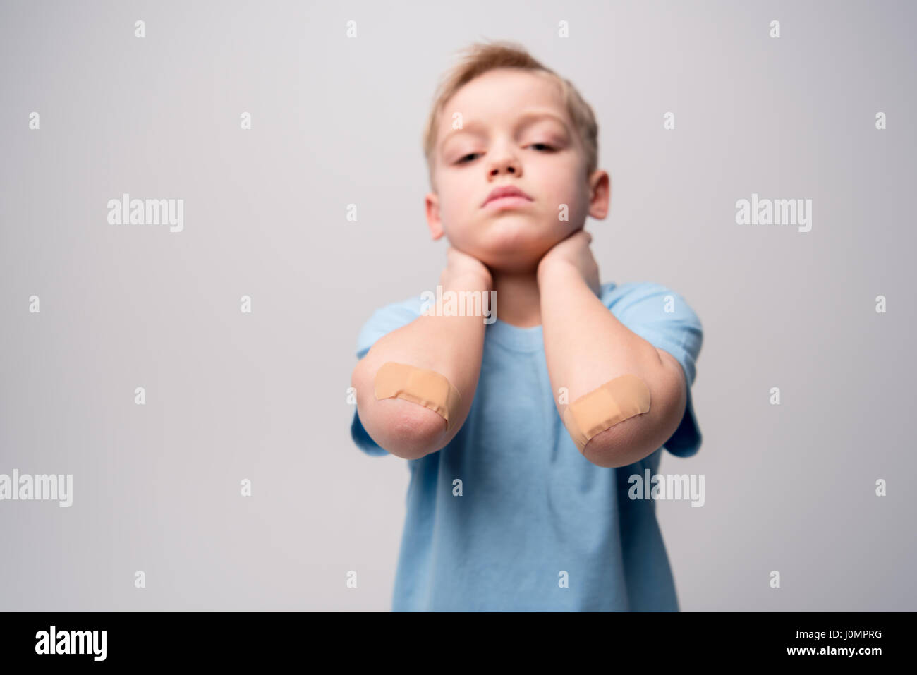 Serious little boy with patches on his injured elbows looking at camera ...