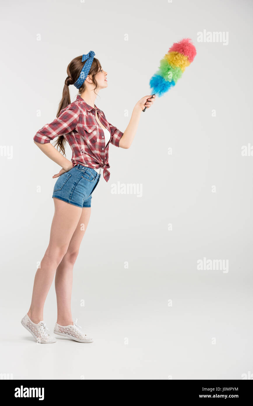 Side view of beautiful young housewife with colorful duster on grey ...