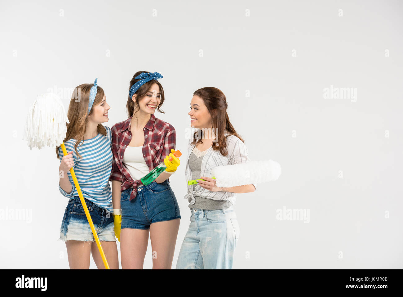 Three beautiful young women holding cleaning supplies and talking on ...