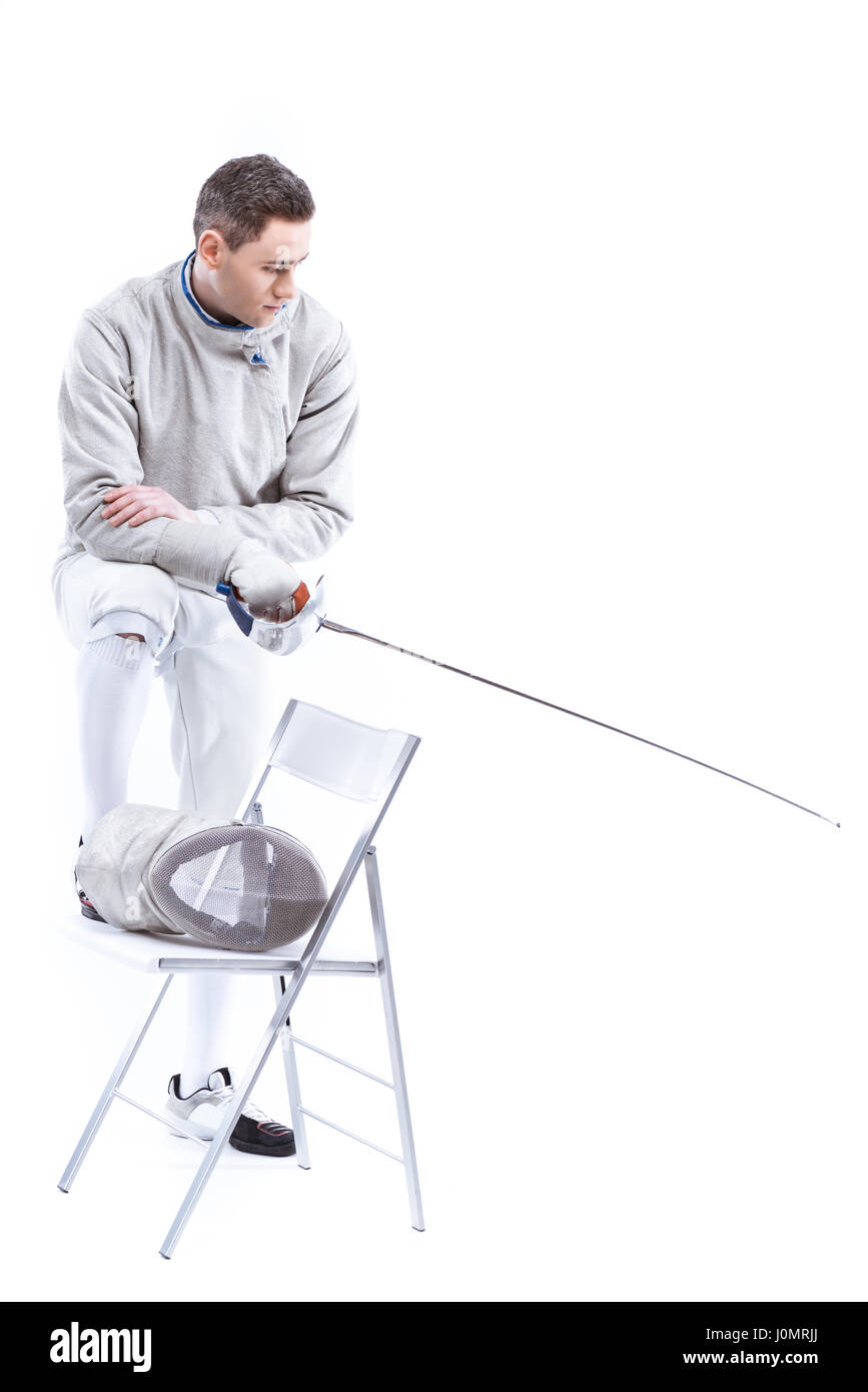 Young pensive man professional fencer holding rapier and looking down ...
