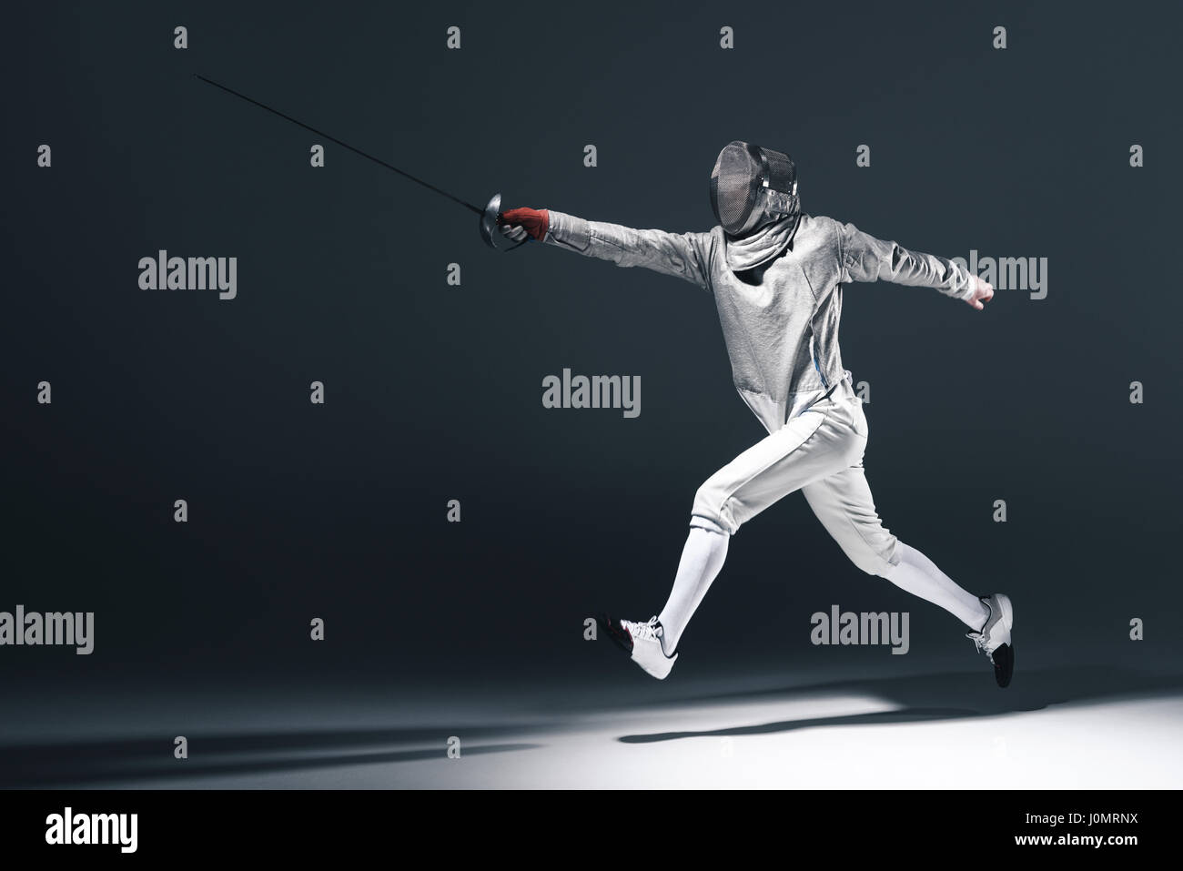 Professional fencer in fencing mask with rapier jumping on grey Stock ...