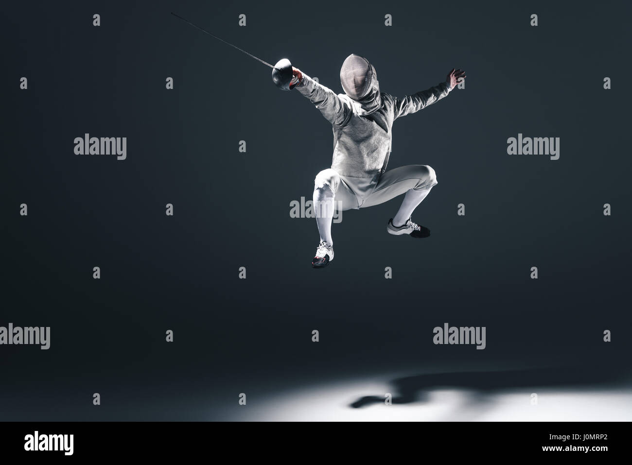 Professional fencer in fencing mask with rapier jumping on grey Stock ...