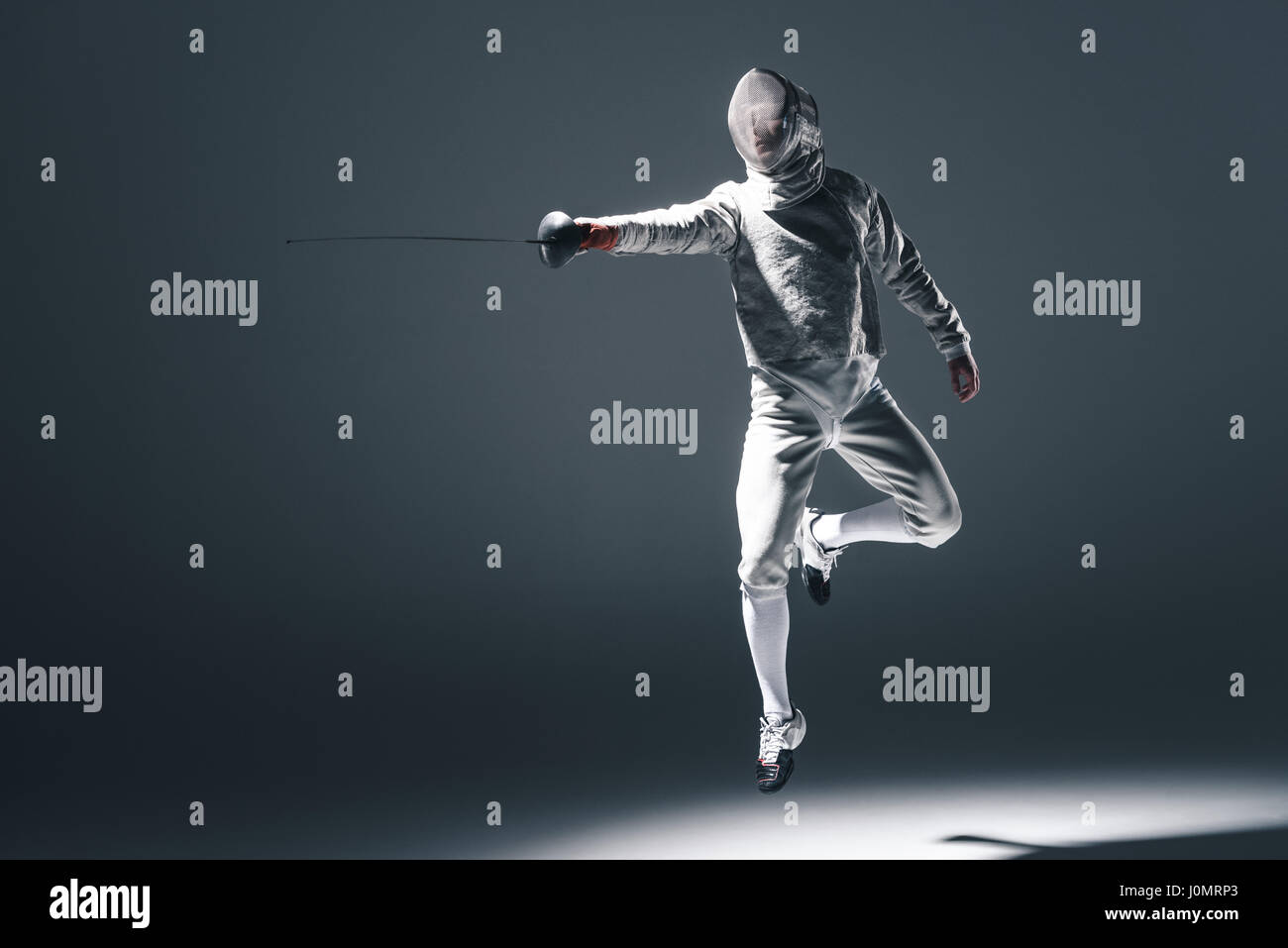 Professional fencer in fencing mask with rapier jumping on grey Stock ...