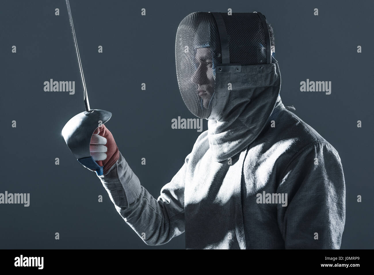 Portrait of professional fencer in fencing mask with rapier on grey ...