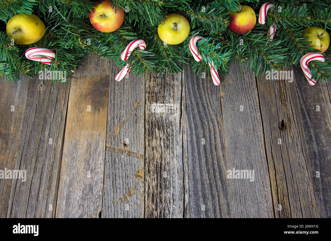 apples and candy canes in Christmas pine garland on weathered wood ...