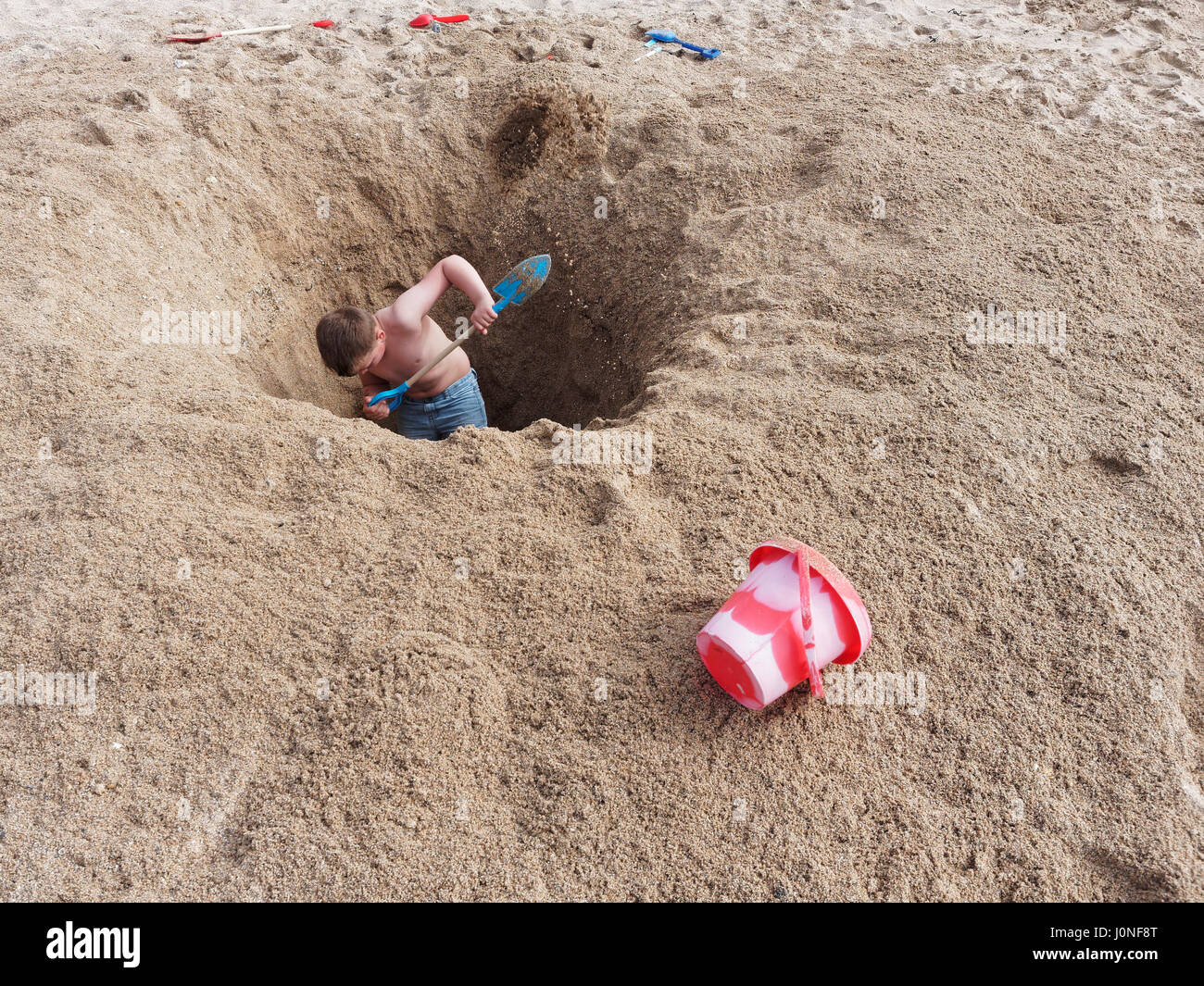 Tiny boy digging large hole with tiny bucket and spade hi-res stock ...