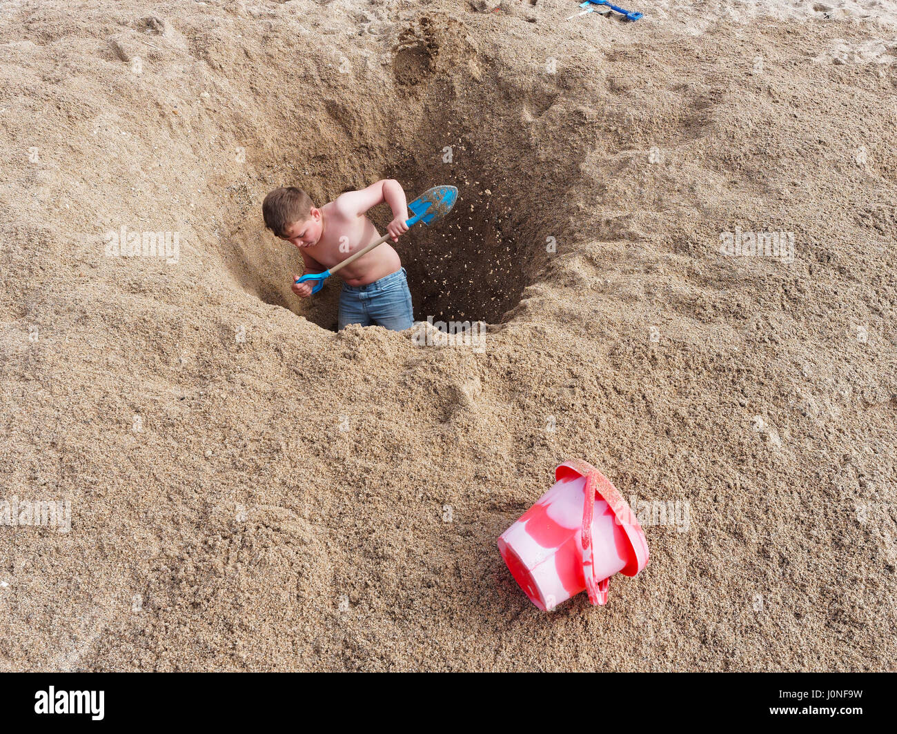 Tiny boy digging large hole with tiny bucket and spade hi-res stock ...