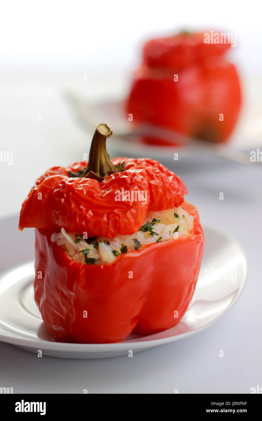 Roasted red peppers stuffed with rice on white plates. Shallow depth of ...