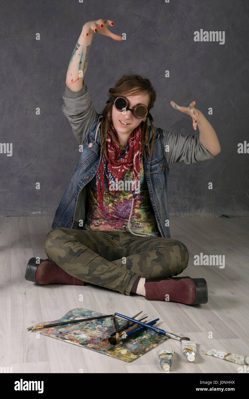 Attractive young female artist with dreadlocks sitting on a floor ...