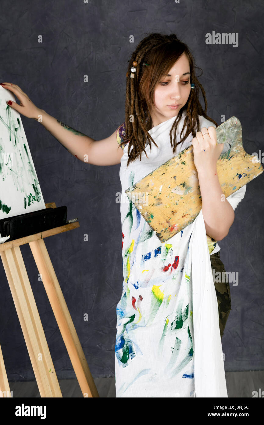 female paint artist posing next to a easel and paints on an canvas ...