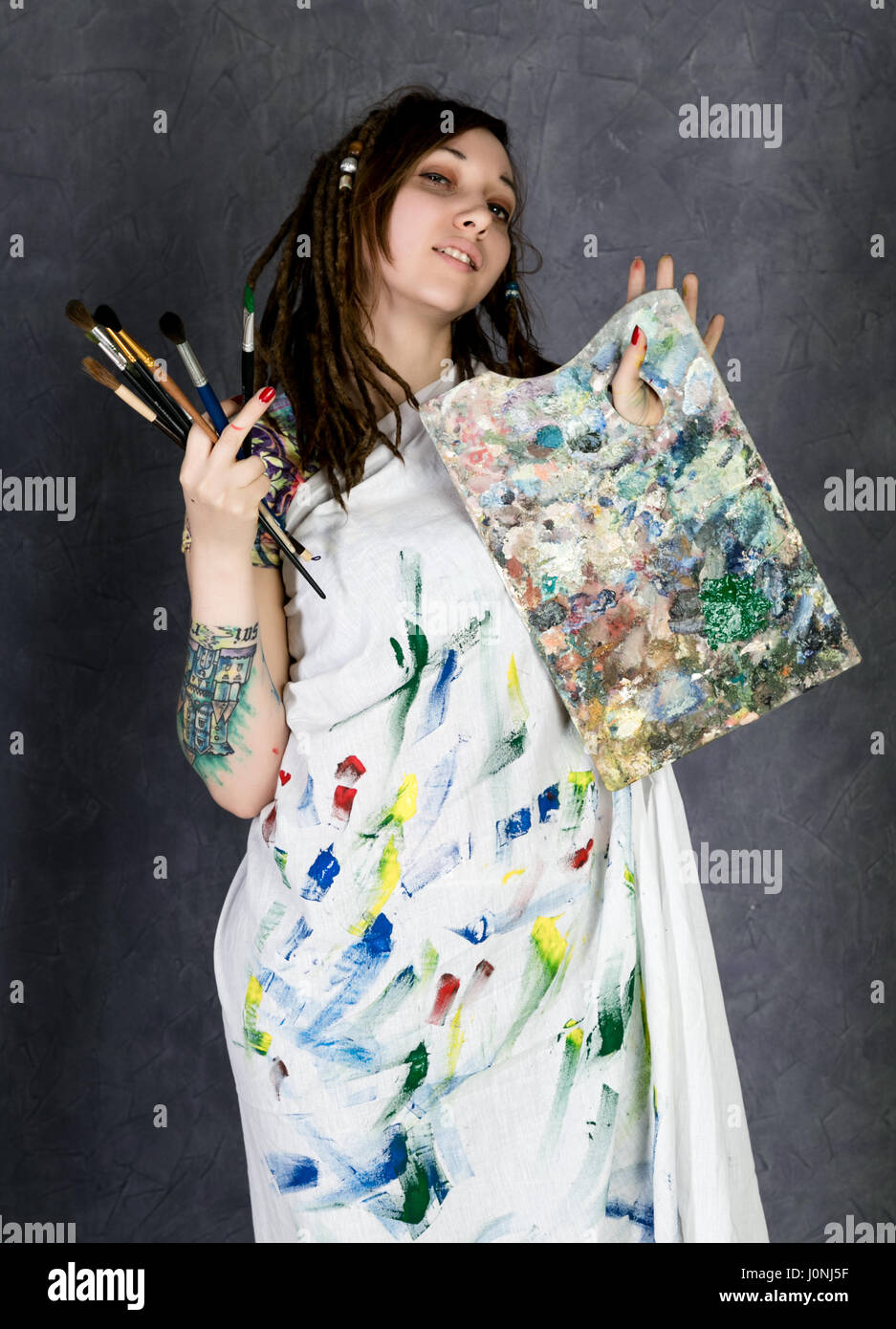 female paint artist posing next to a easel and paints on an canvas ...
