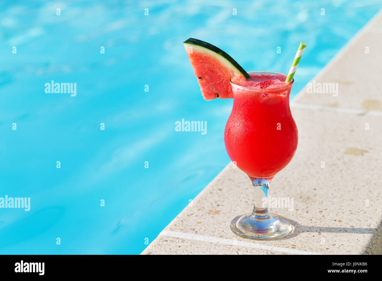Glass of fresh watermelon smoothie juice drink on border of a swimming ...