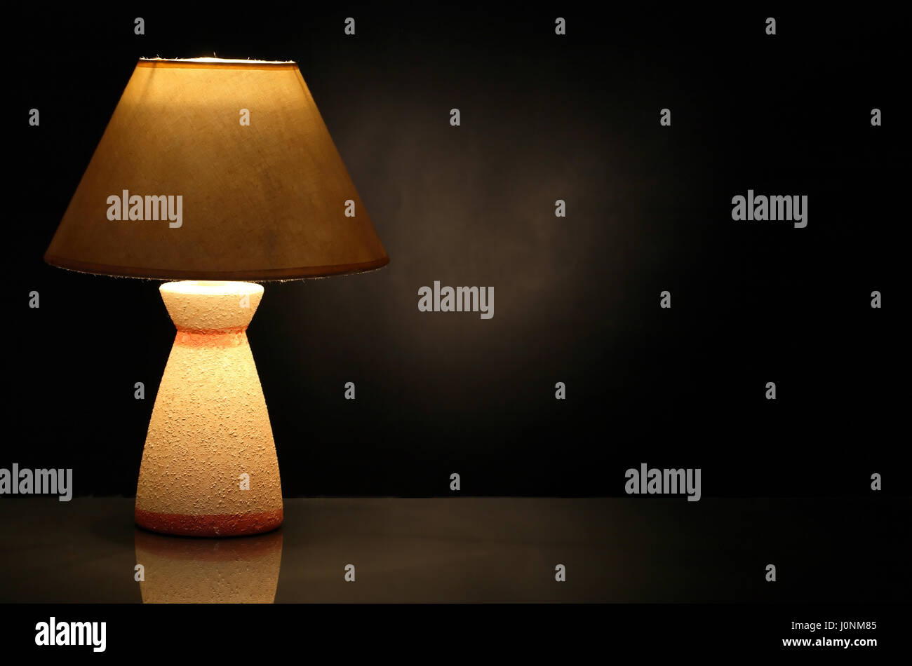 Luminous desk lamp with lampshade on dark glass surface with reflection ...