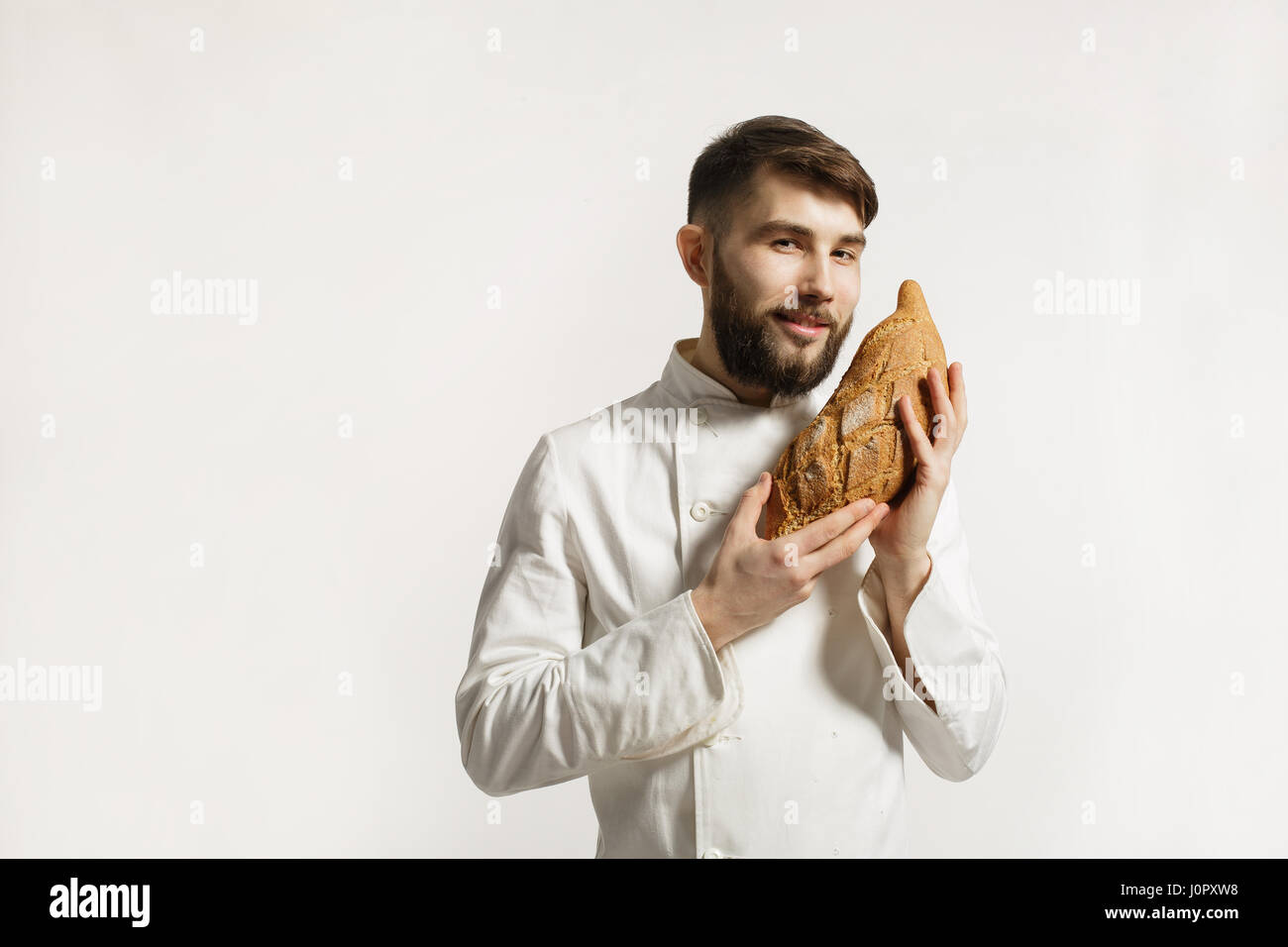 Handsome smiling BAKER smelling a freshly baked loaf in the kitchen of ...