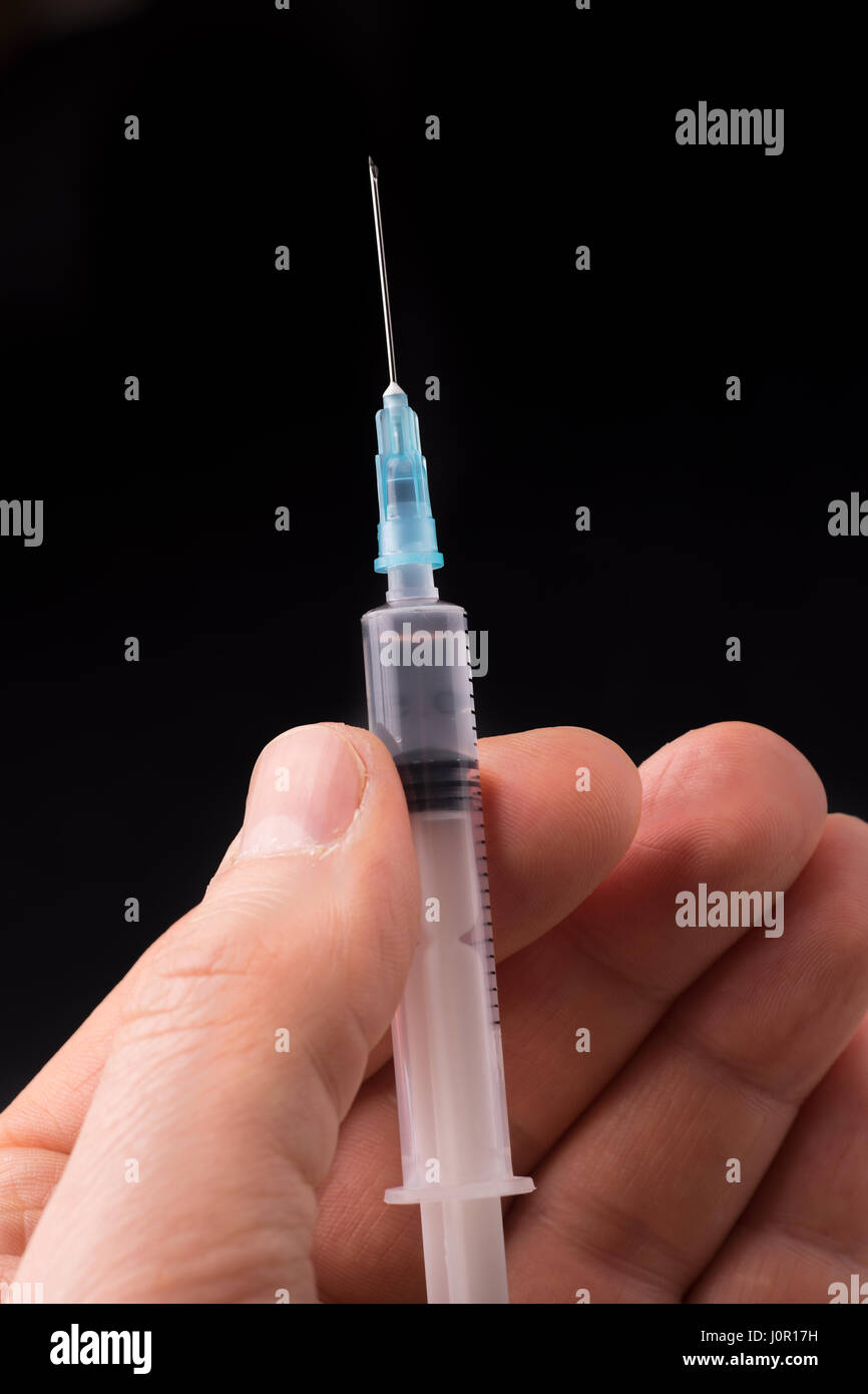 Hand holding a syringe, the syringe is filled with clear liquid and the ...